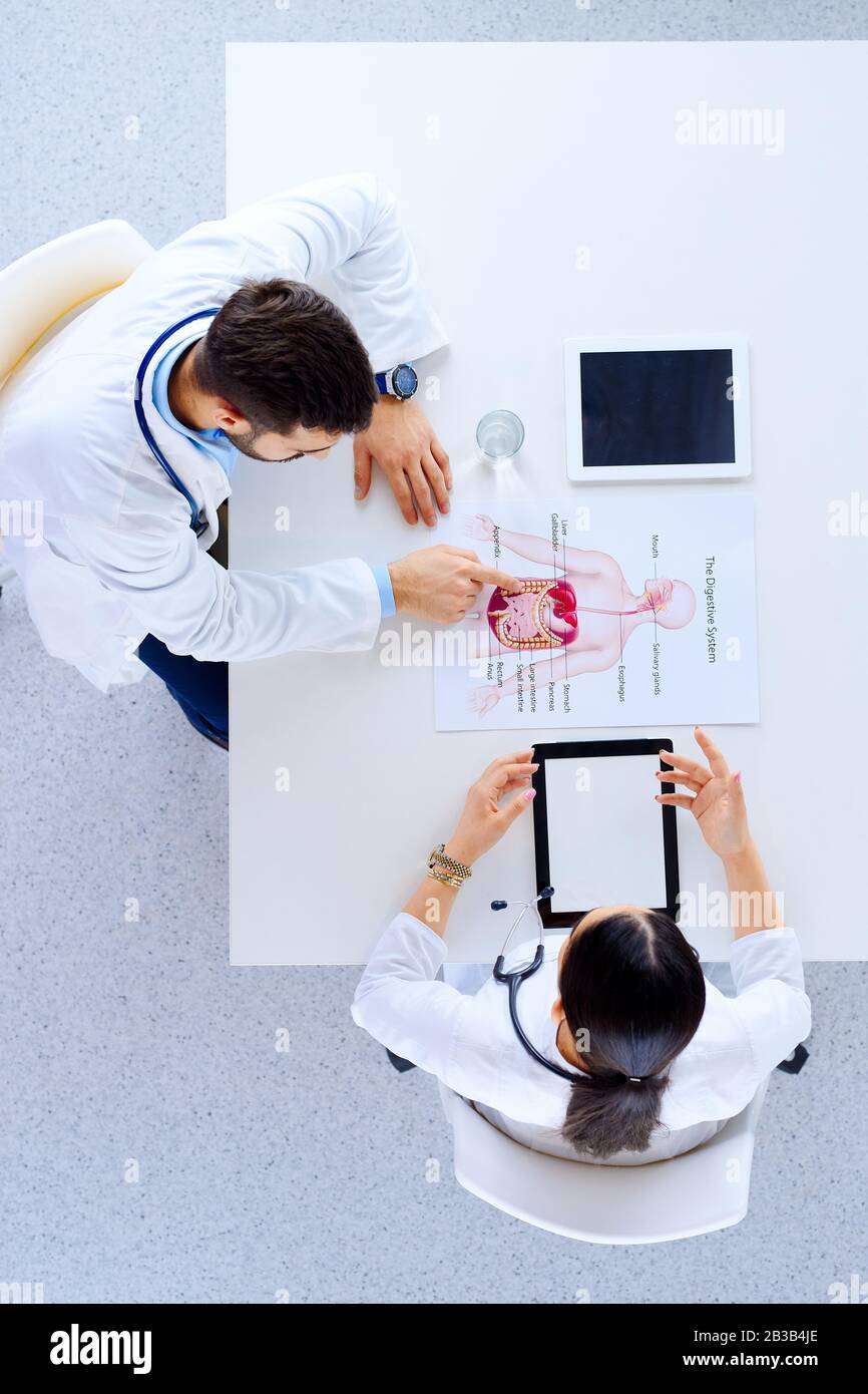 Medical team of doctors sitting and discussing at table with tablets ...