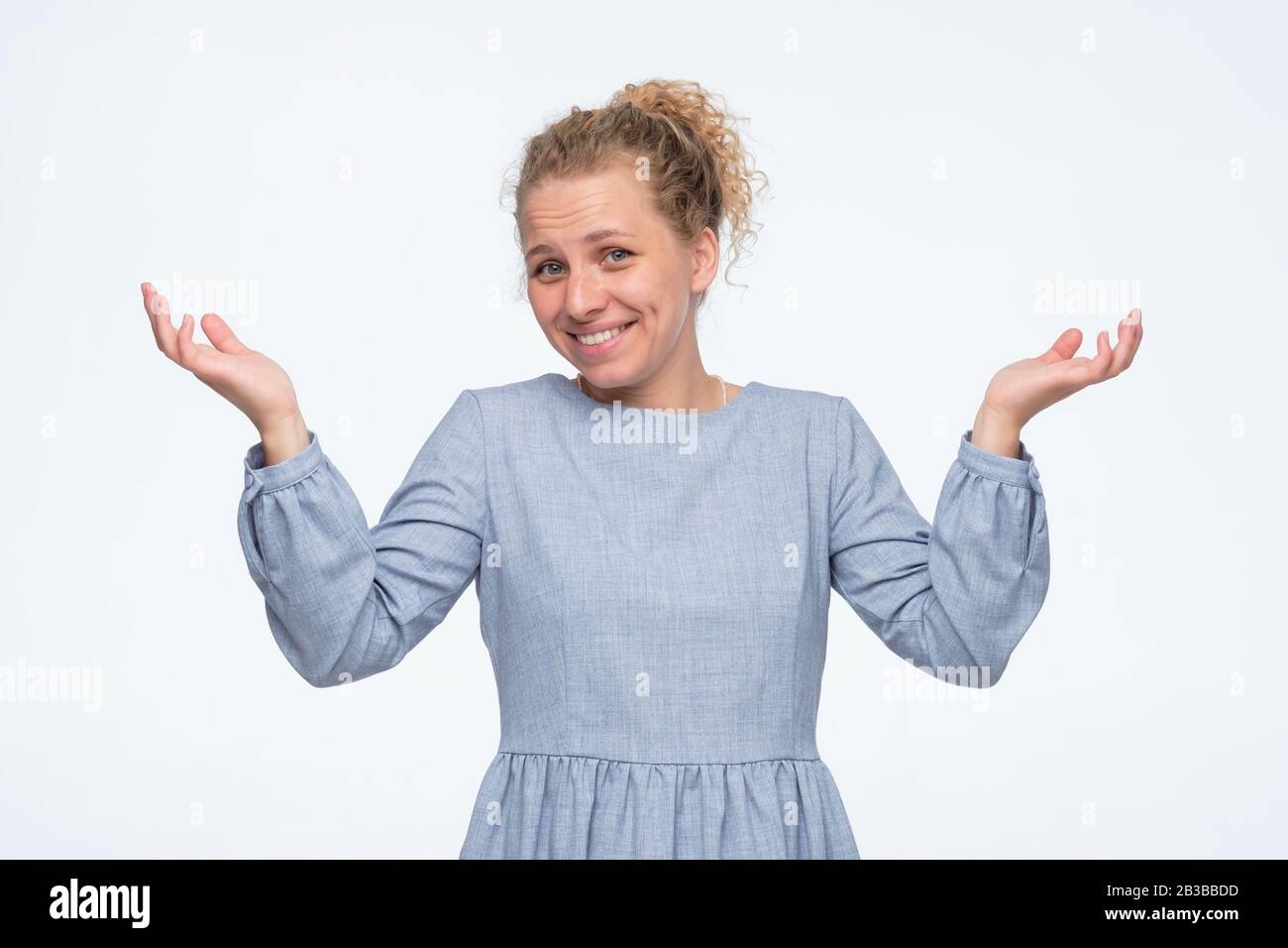 Carefree happy clueless young woman in dress shrugging with hands ...