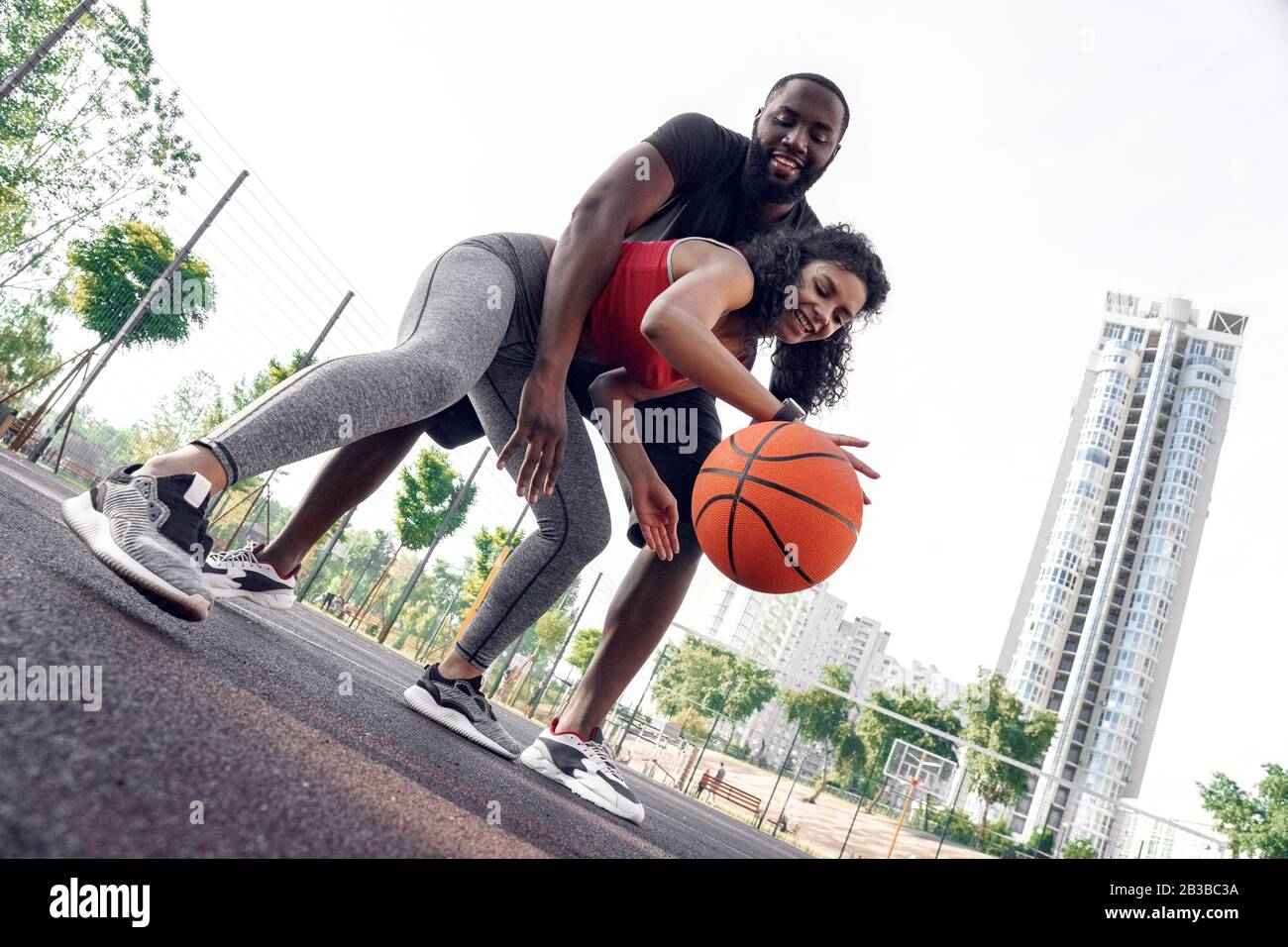 Outdoors Activity. African couple on basketball court girl dribbling ...