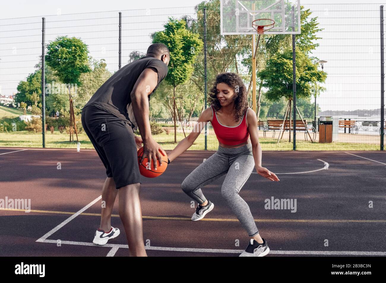 Outdoors Activity. African couple on basketball court guy dribbling ...