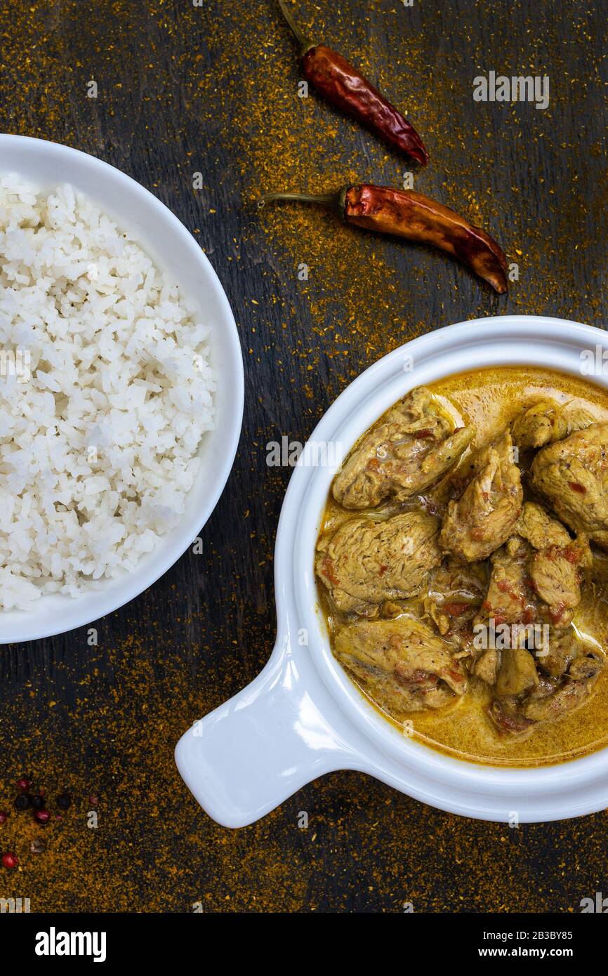 Orange spicy chicken curry and rice in simple white plates on a dark ...