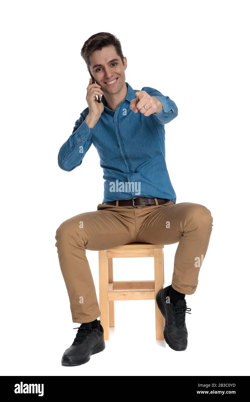 happy young man talking on the phone and pointing finger, sitting ...
