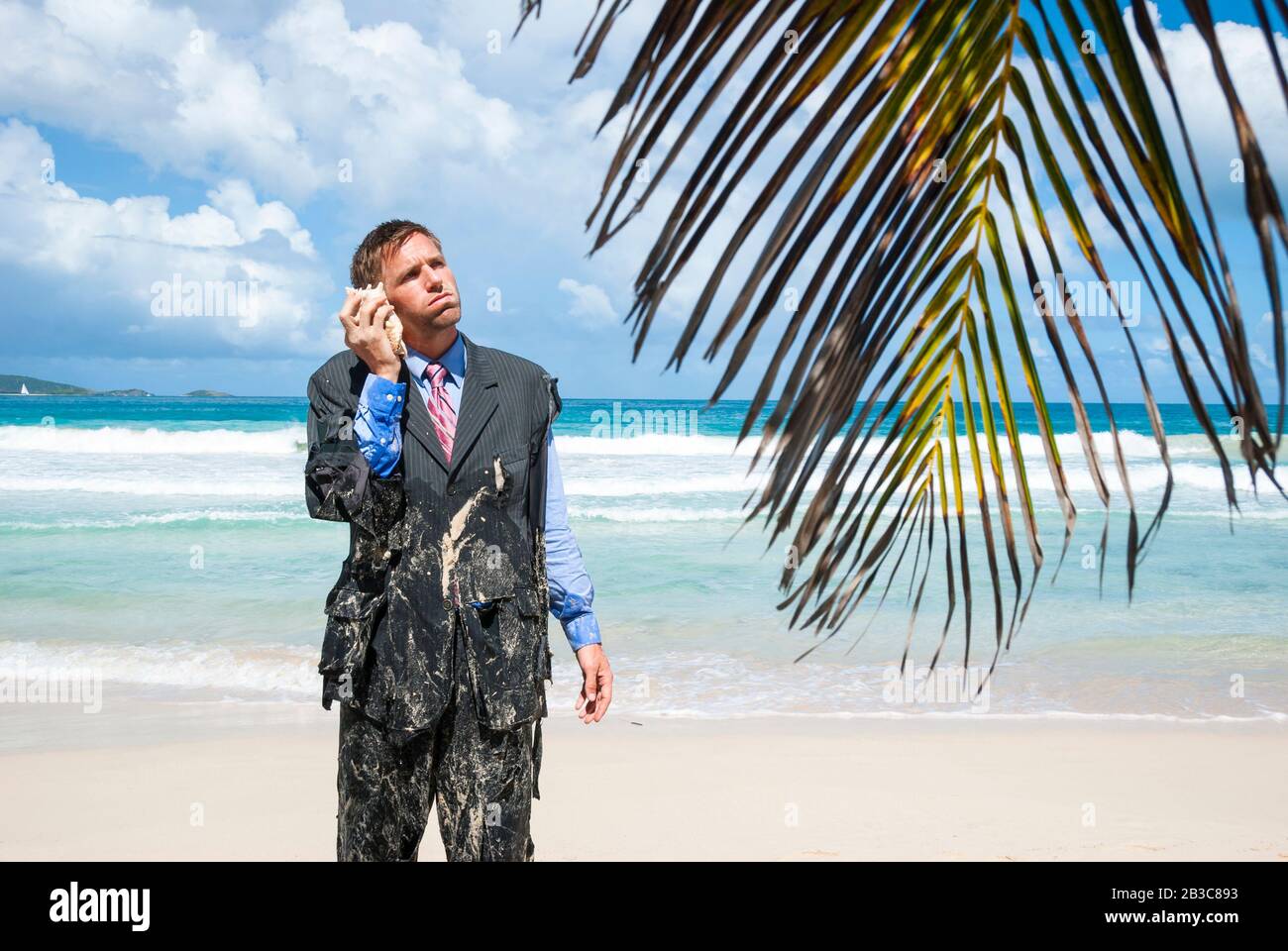 Stranded castaway businessman standing on the beach in his ragged suit ...