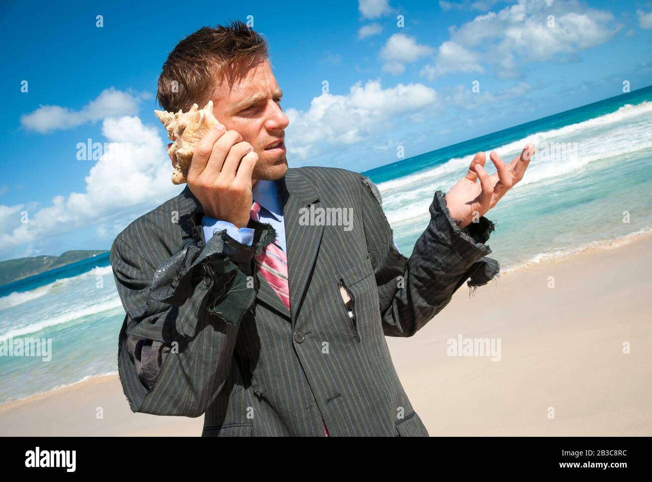 Stranded castaway businessman standing on the beach in his ragged suit ...