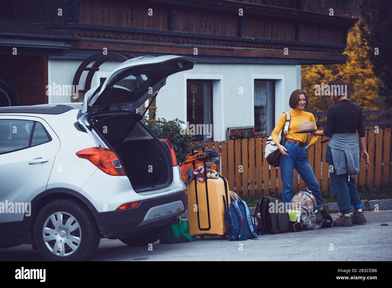 road trip - Two happy smiling girls load car trunk Stock Photo - Alamy