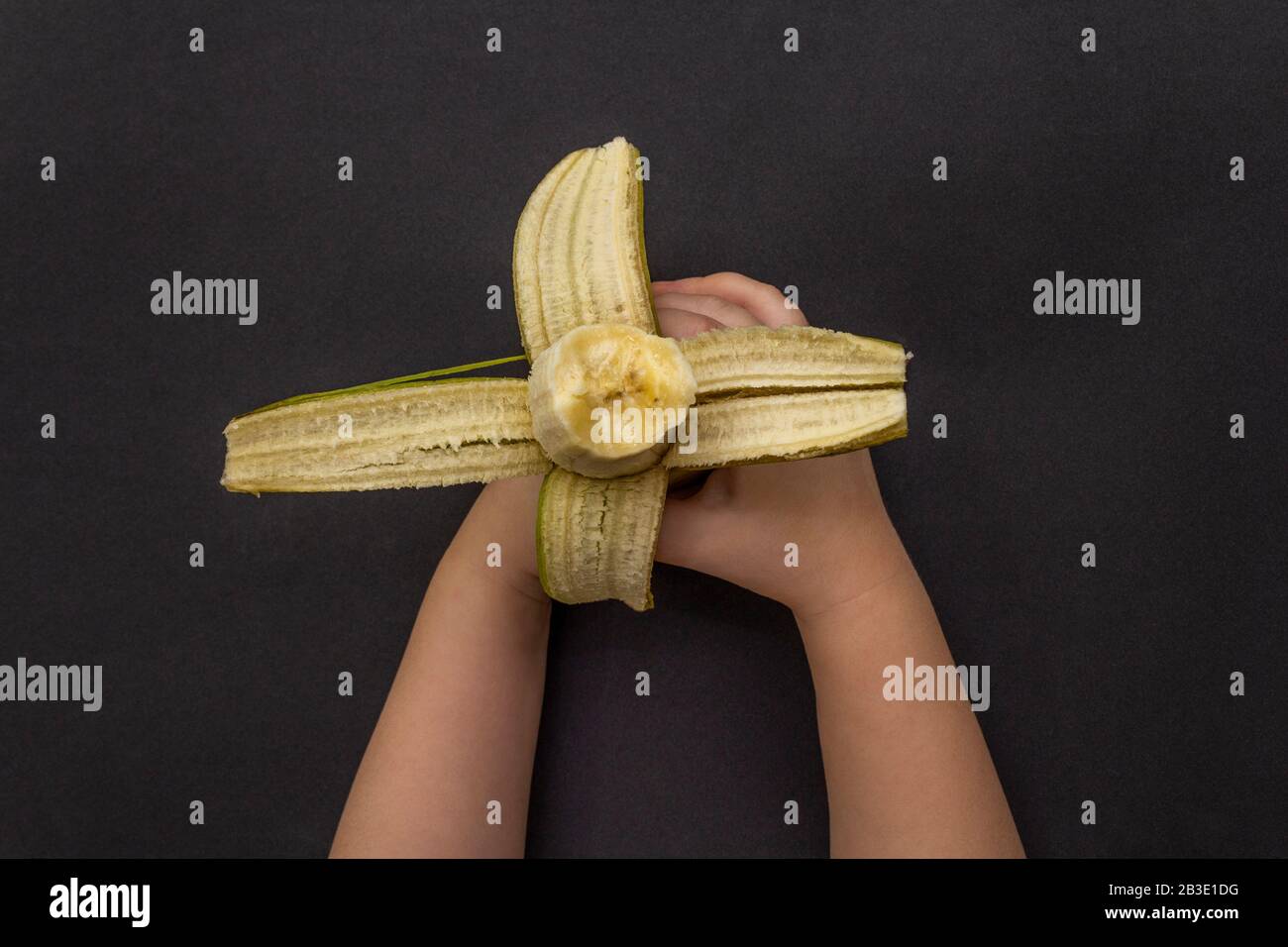 One bitten banana in children's hands. Black background, top view ...