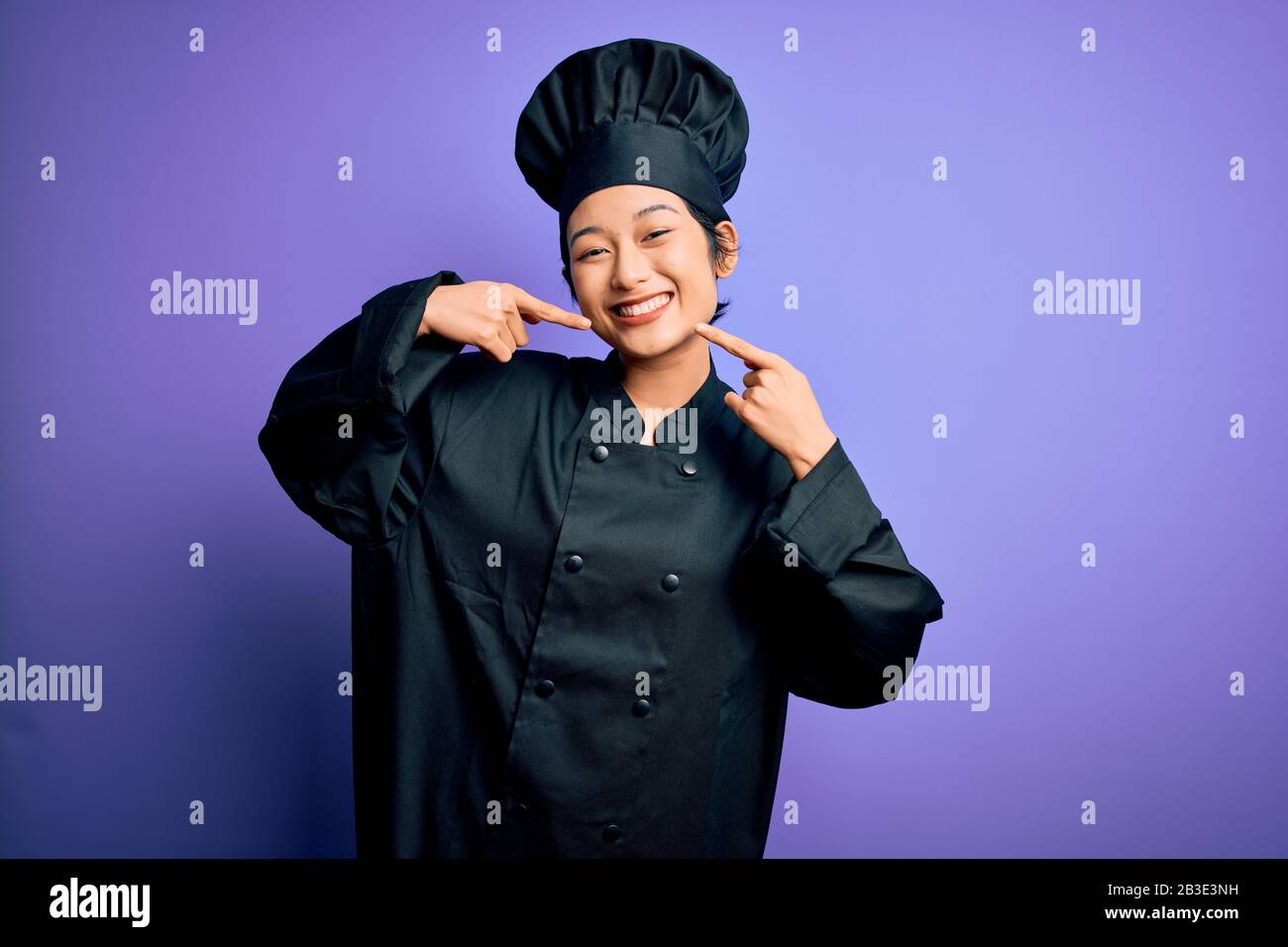Young beautiful chinese chef woman wearing cooker uniform and hat over ...