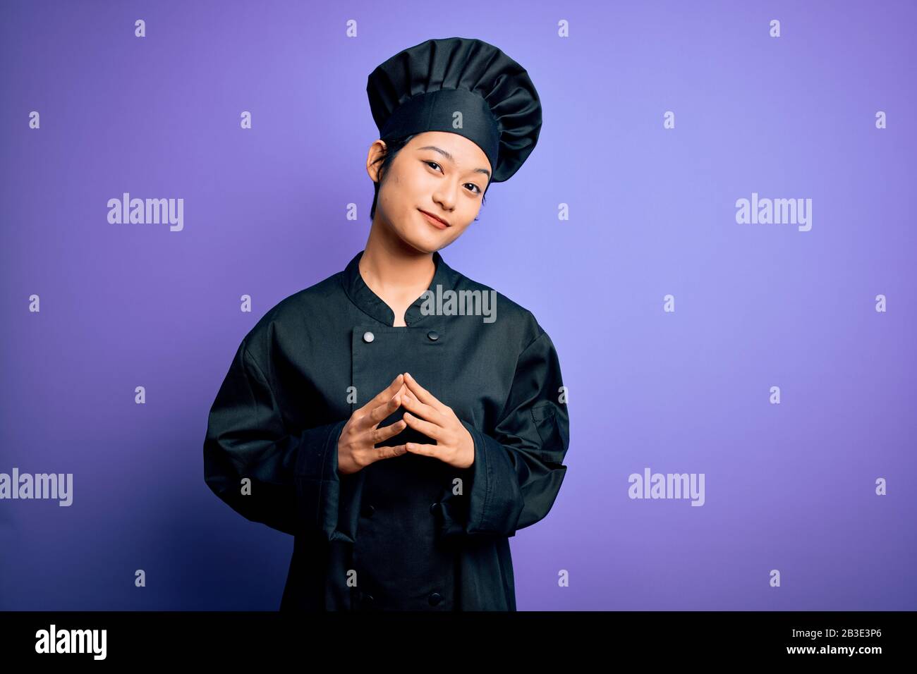 Young beautiful chinese chef woman wearing cooker uniform and hat over ...
