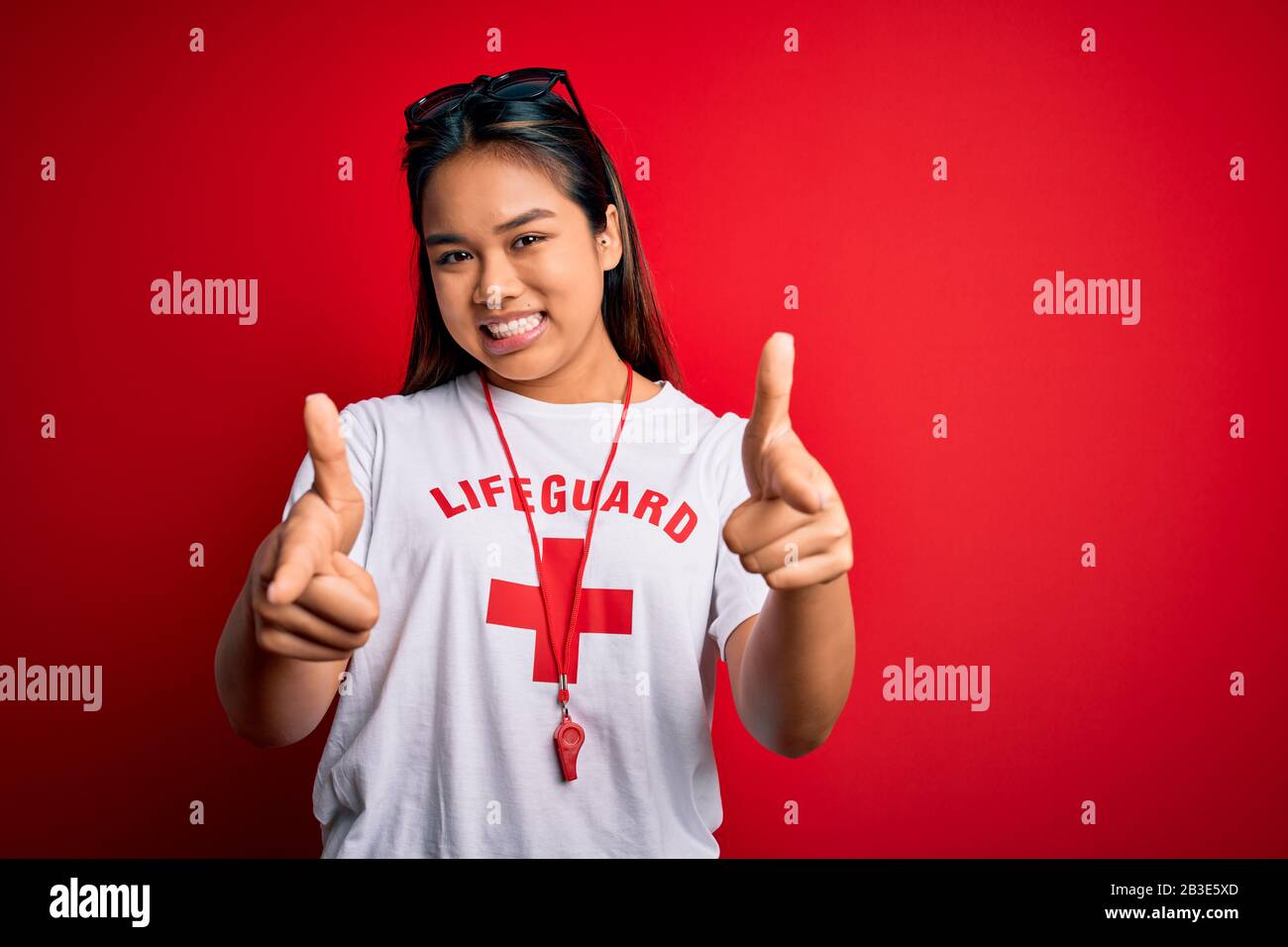 Young asian lifeguard girl wearing t-shirt with red cross using whistle ...
