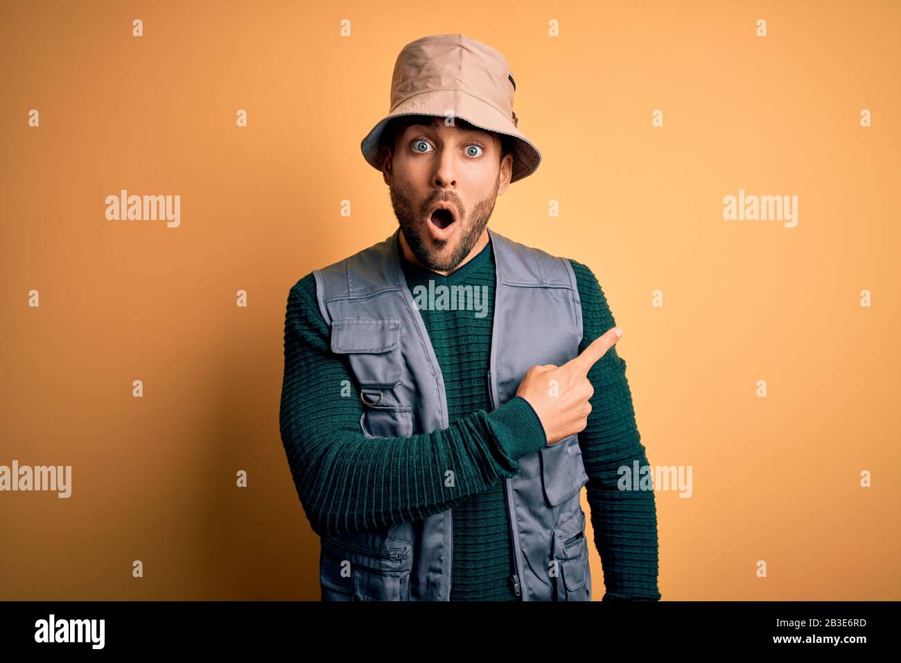 Handsome tourist man with beard on vacation wearing explorer hat over ...