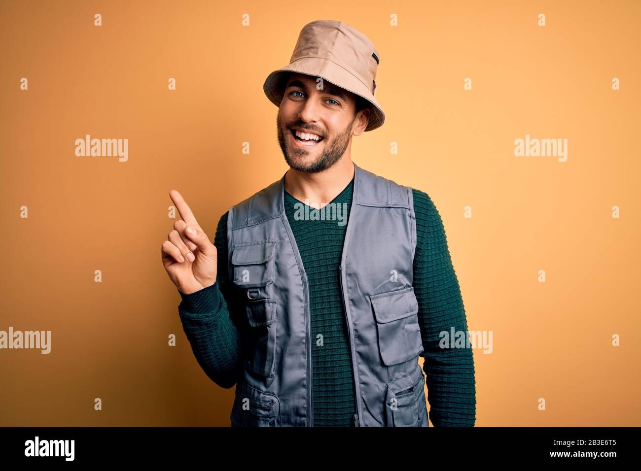 Handsome tourist man with beard on vacation wearing explorer hat over ...