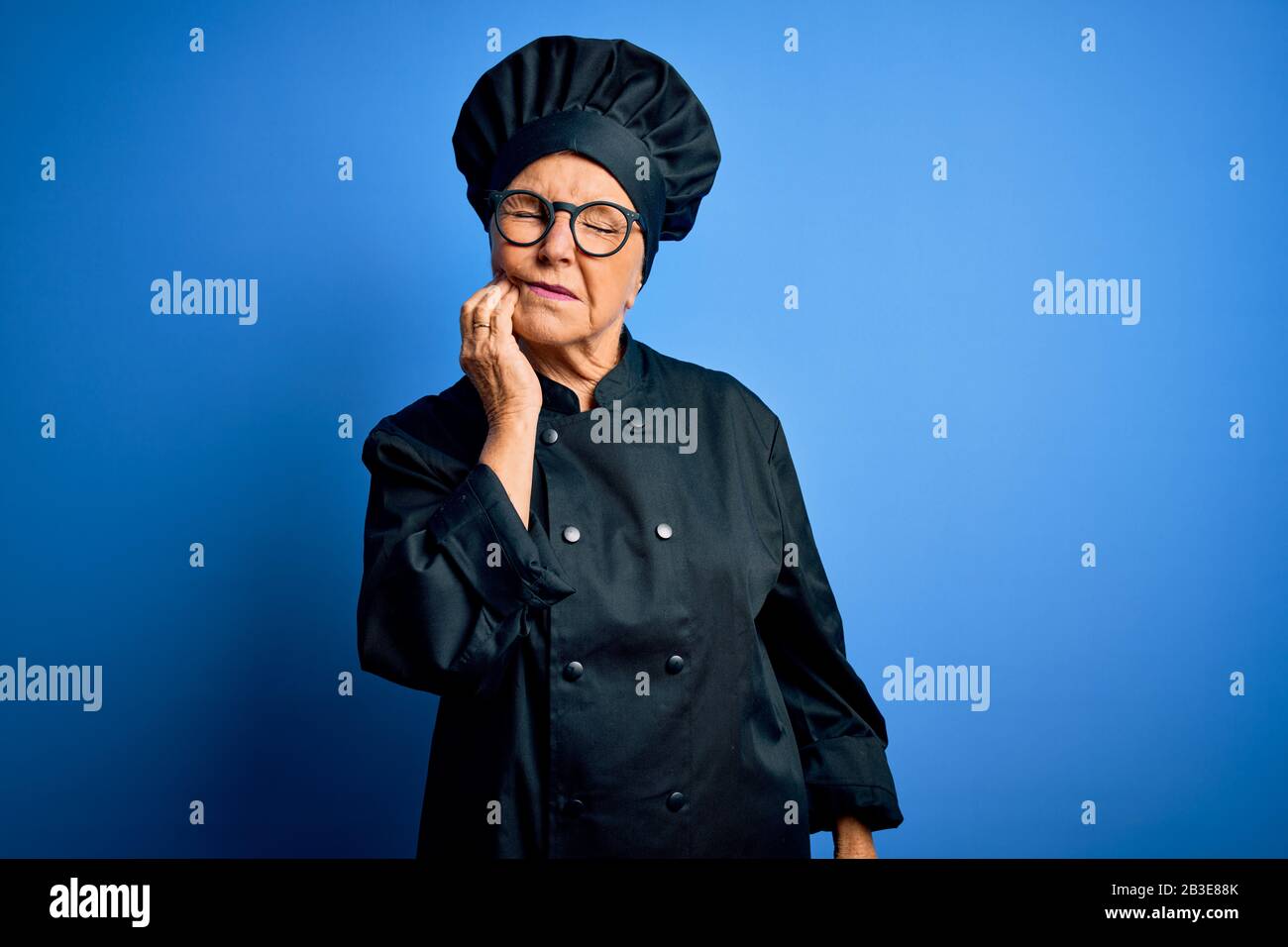 Senior beautiful grey-haired chef woman wearing cooker uniform and hat ...