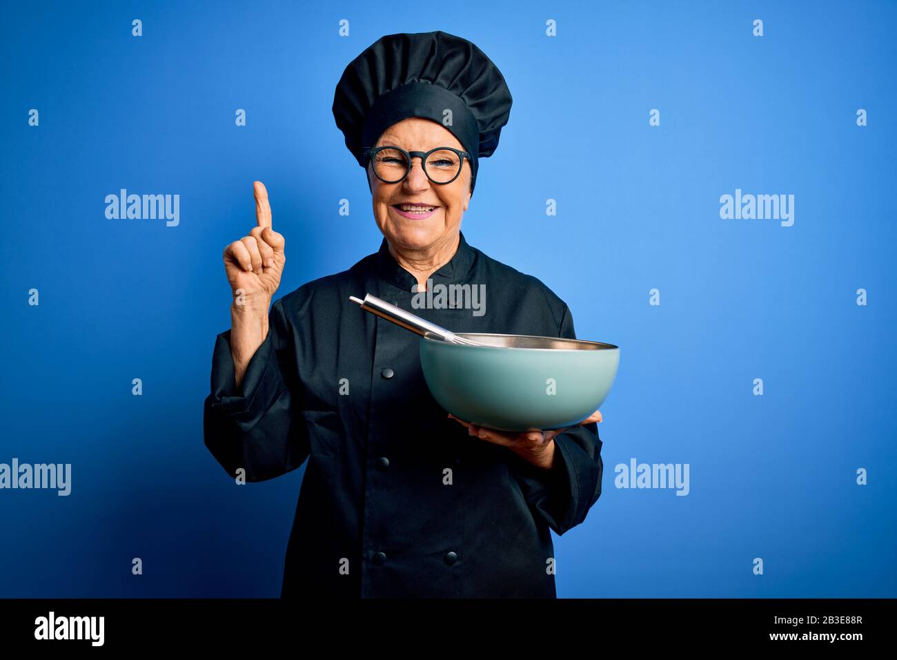 Senior beautiful grey-haired chef woman wearing cooker uniform and hat ...