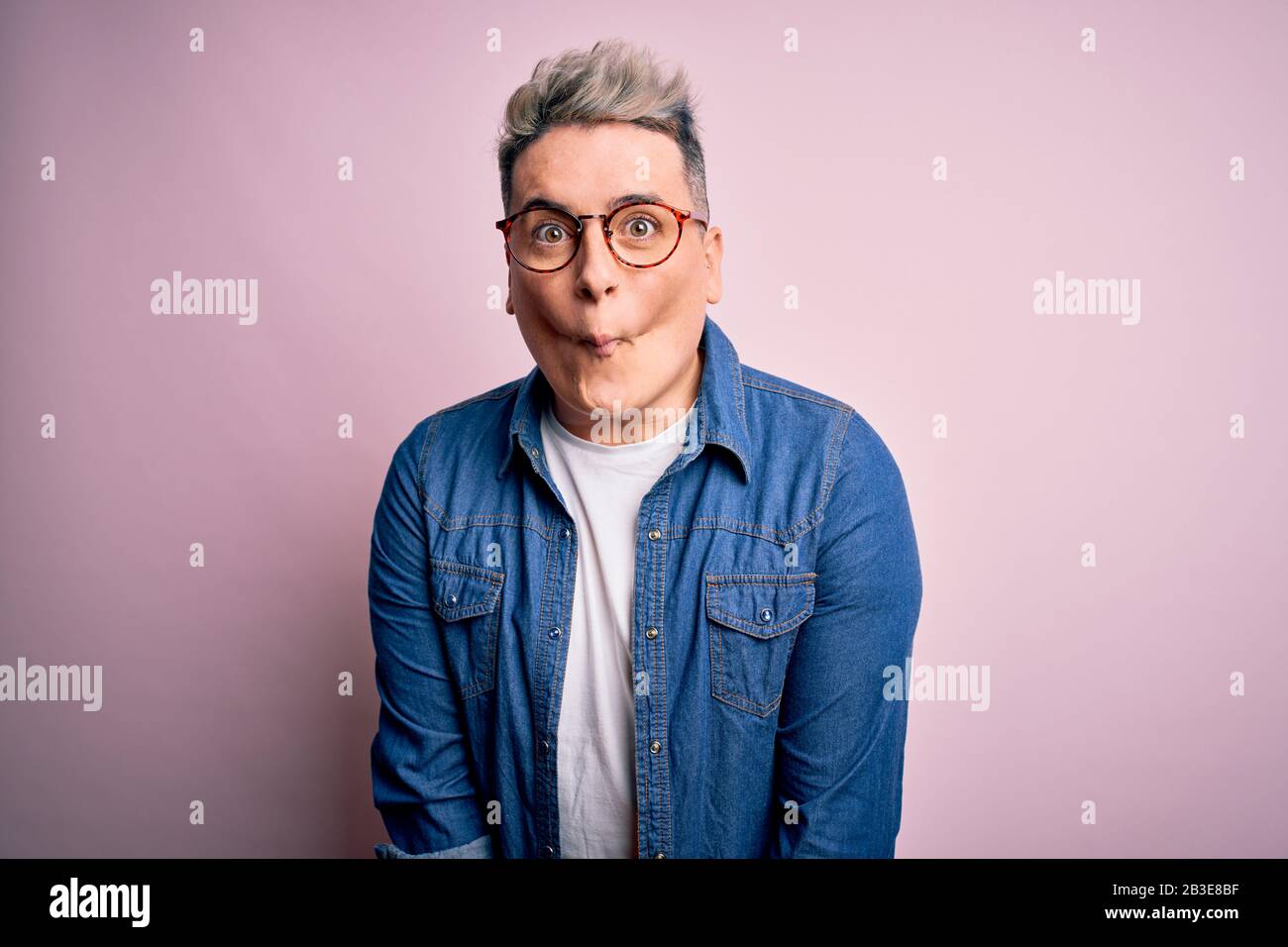 Young handsome modern man wearing glasses and denim jacket over pink ...