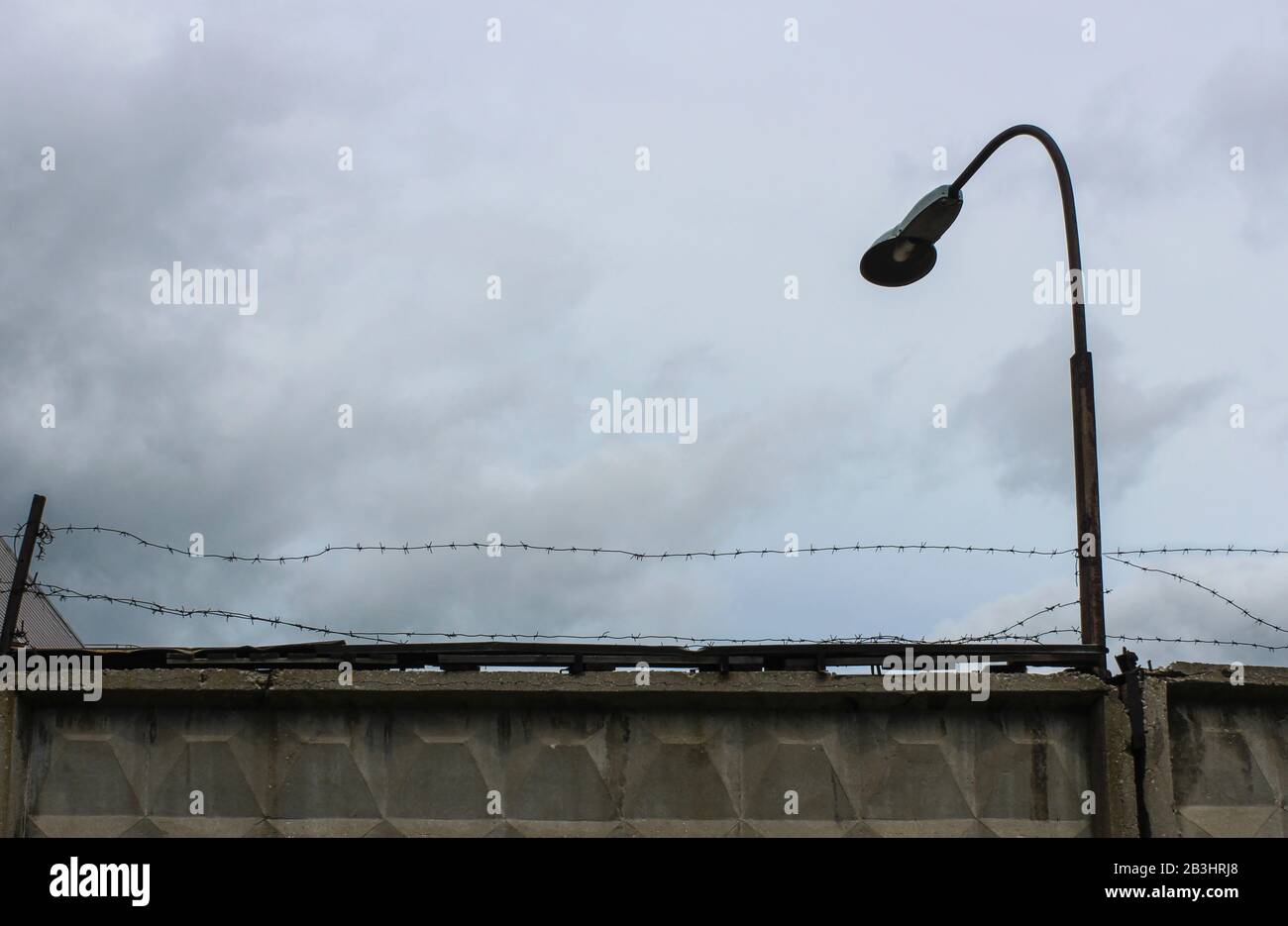Concrete fence with barbed wire and a lantern against a cloudy sky ...