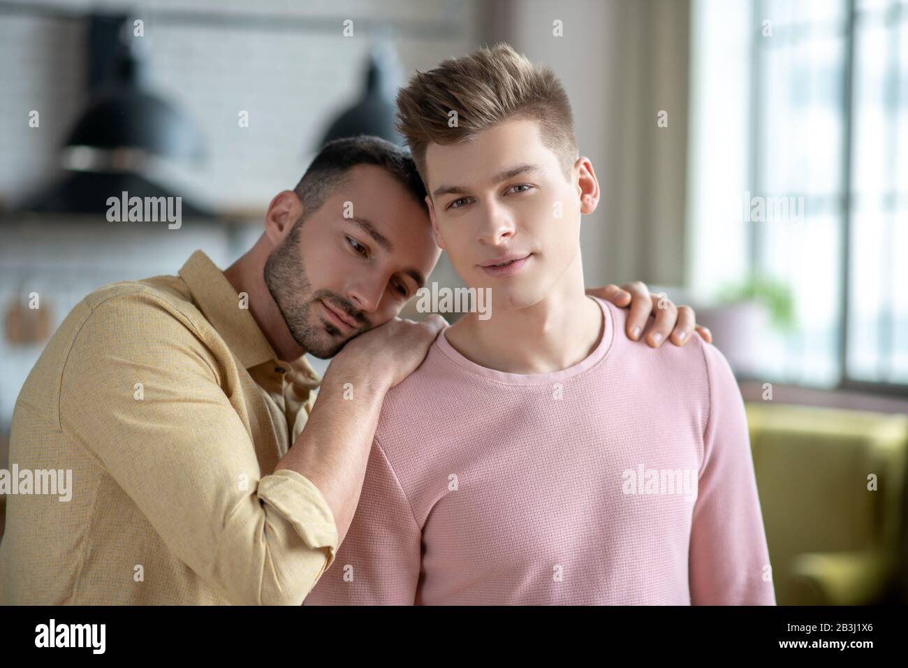 Dark-haired man in orange shirt putting hands on his partners shoulder ...