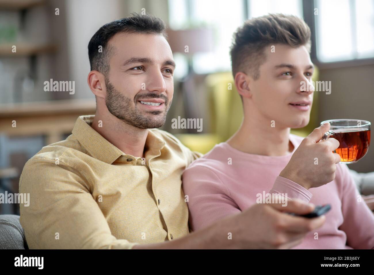 Two young men having tea and watching tv together Stock Photo - Alamy