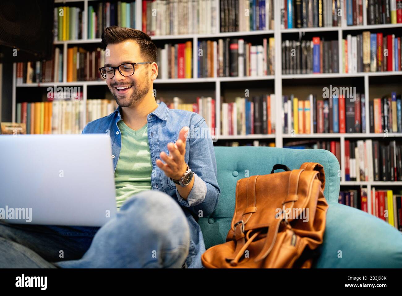 Happy student working on laptop in library Stock Photo - Alamy