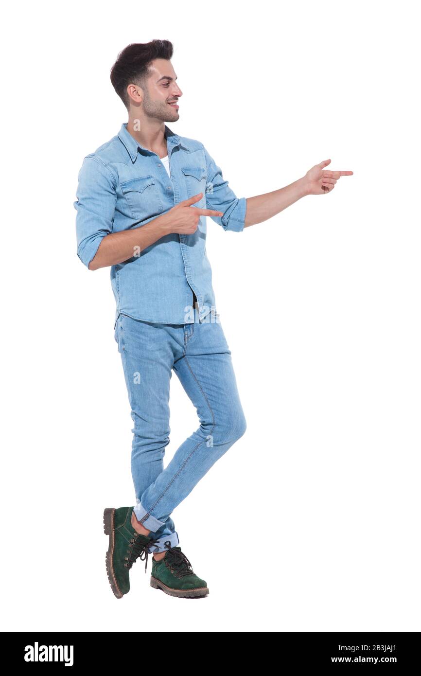 relaxed young man greeting and pointing fingers to side, wearing denim ...