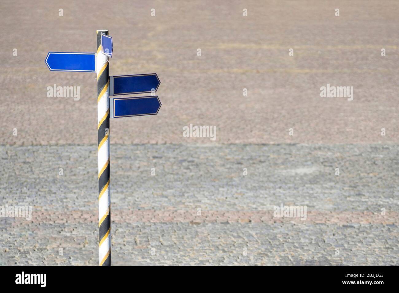 Striped road sign with blank direction arrows against stone pavement ...