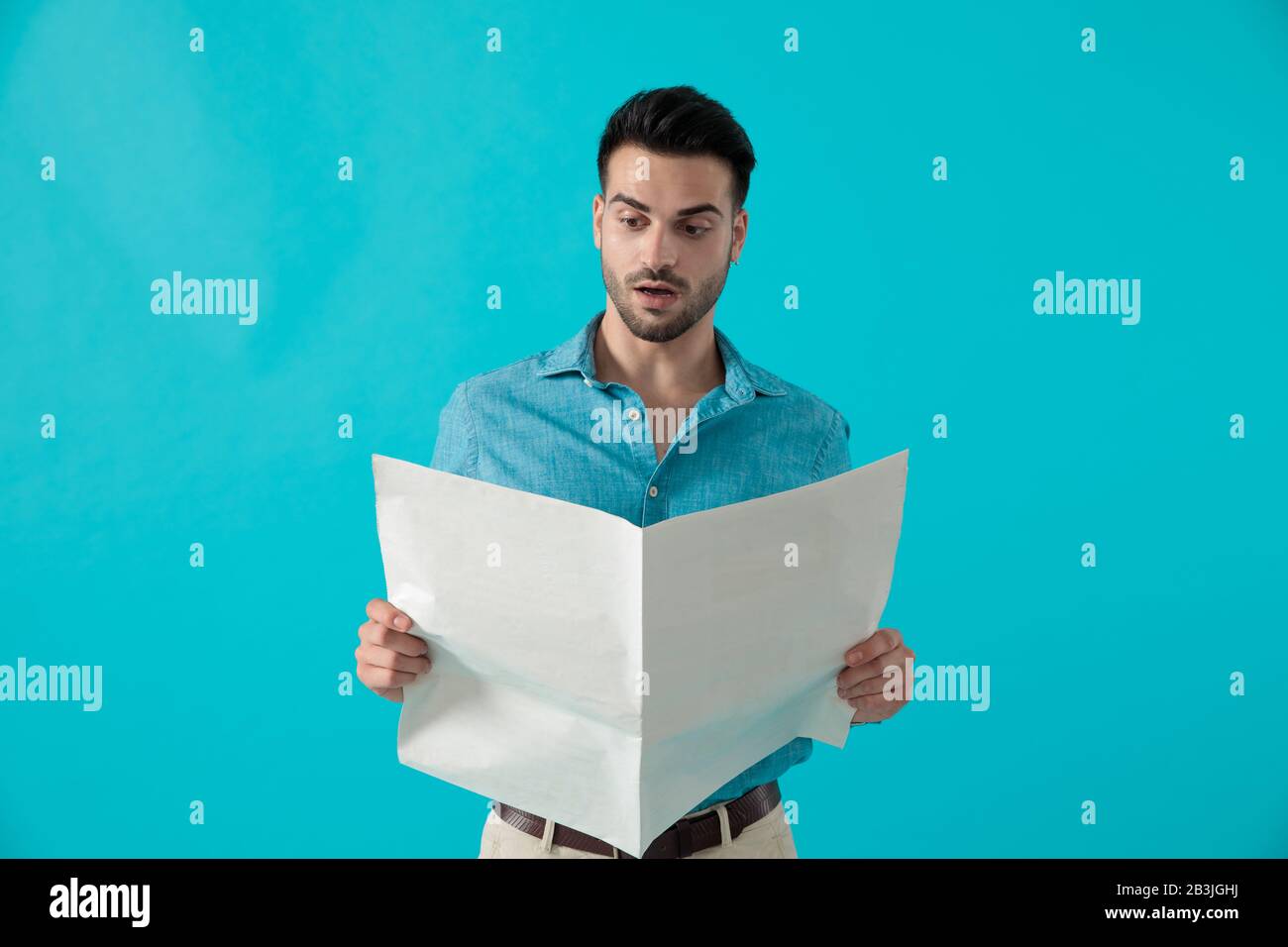 attractive casual man in blue shirt is standing and reading the ...