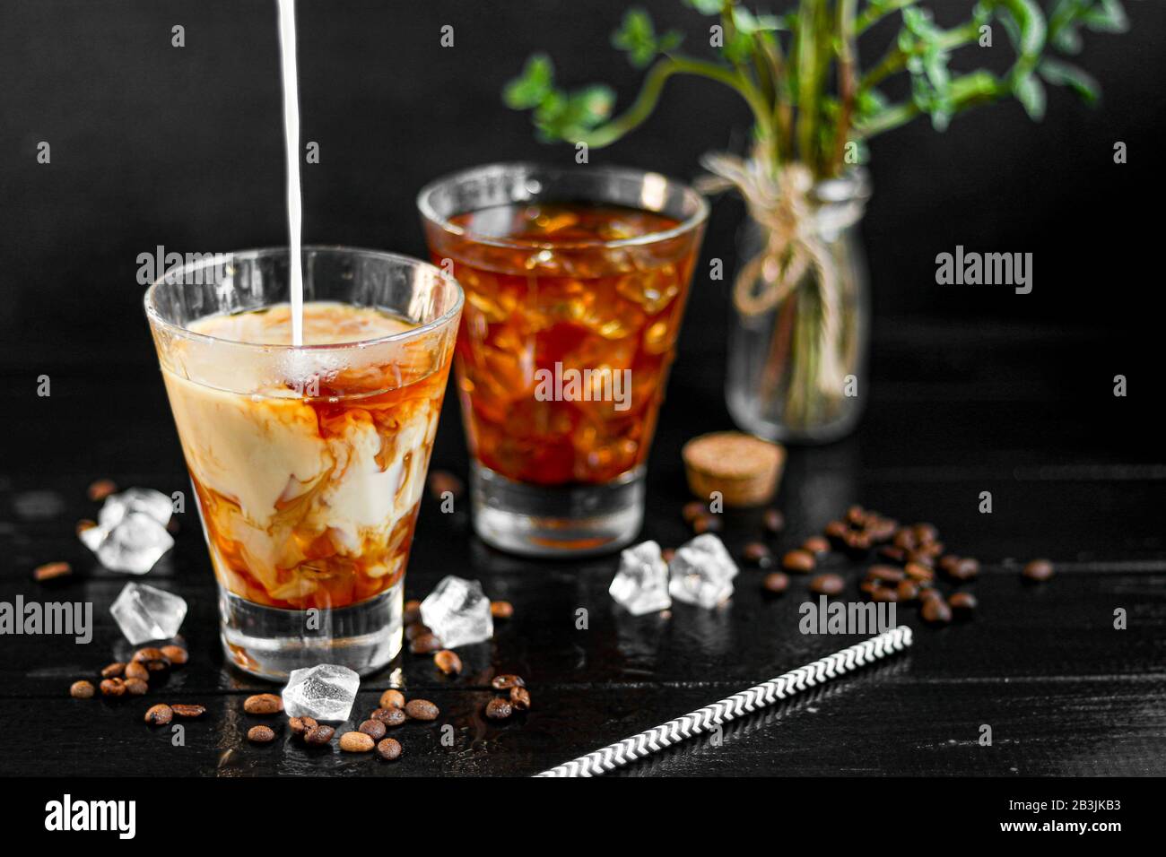 Iced coffee in a tall glass with milk and pieces of ice. On a dark ...