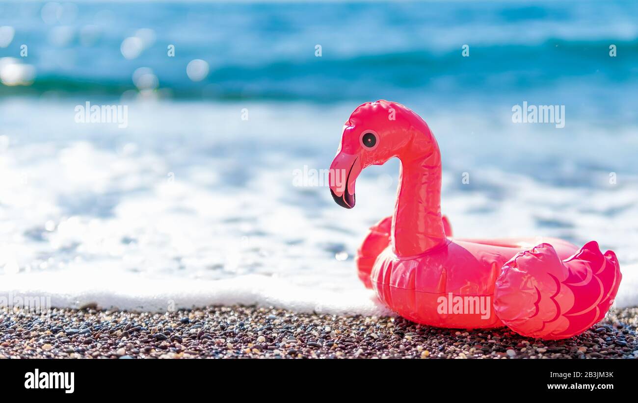 Inflatable pink flamingos on beach with white foam of sea wave. Summer ...