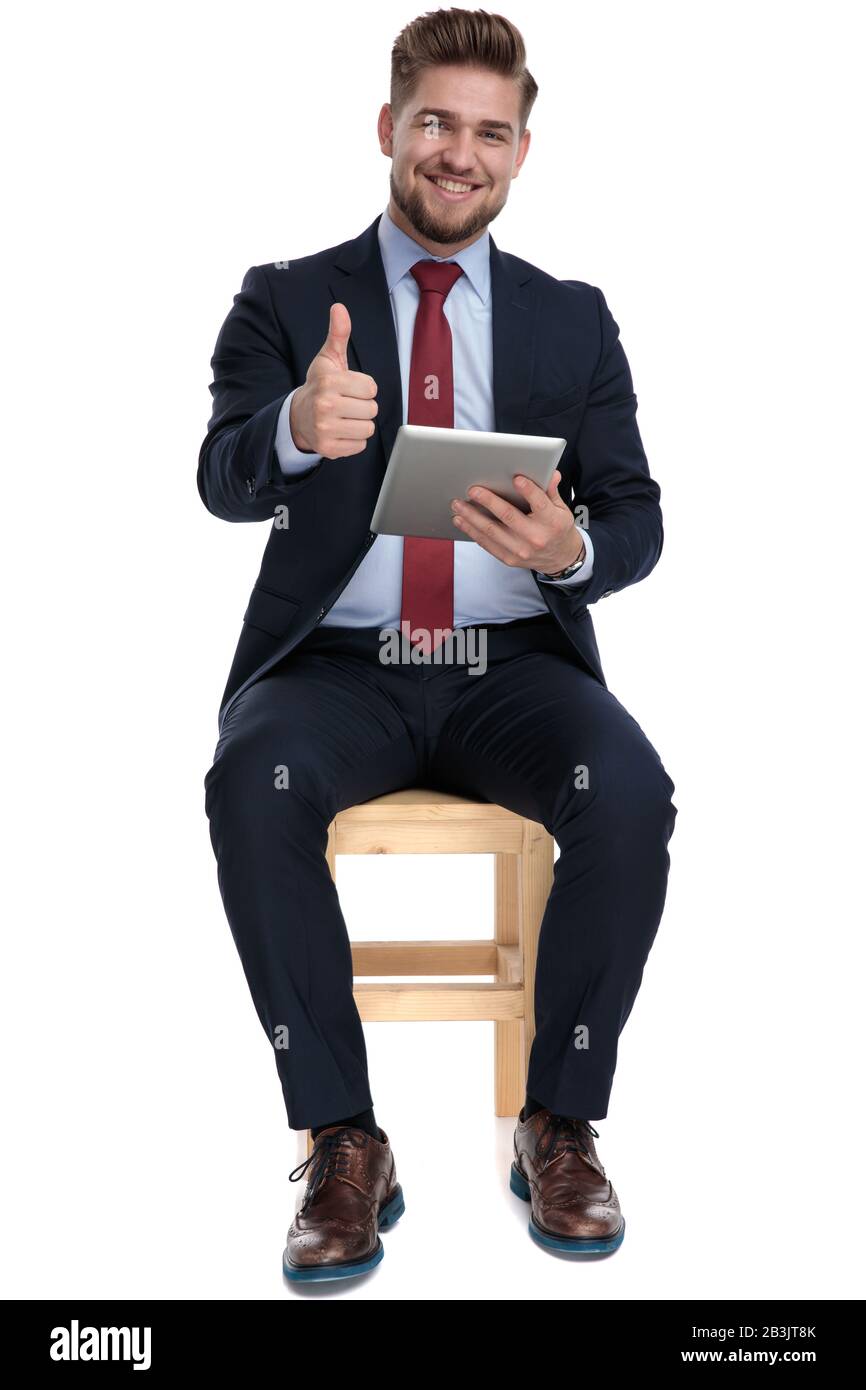 optimistic young man smiling, holding tab and making thumbs up sign ...