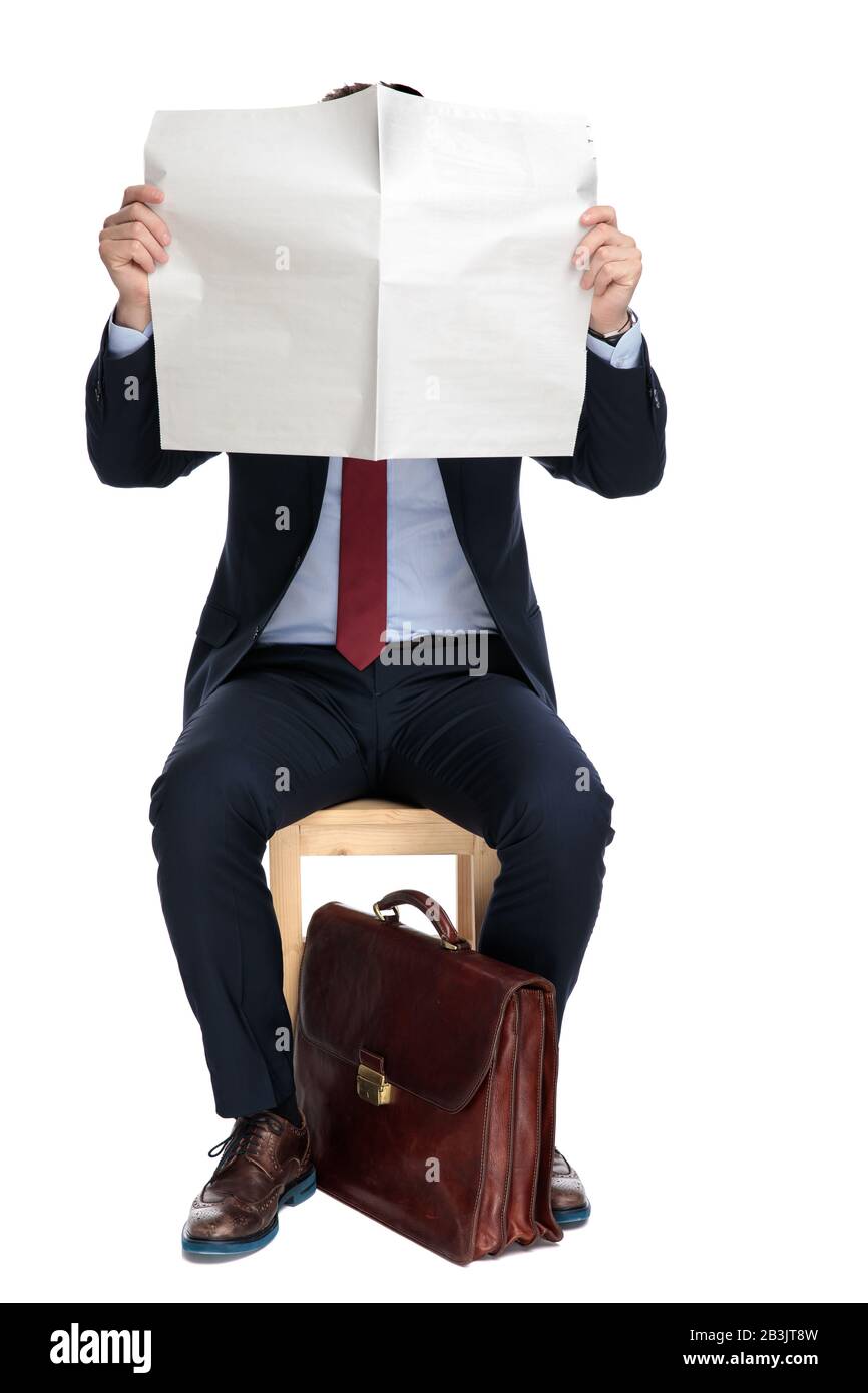 young businessman hiding behind newspaper and sitting isolated on white ...