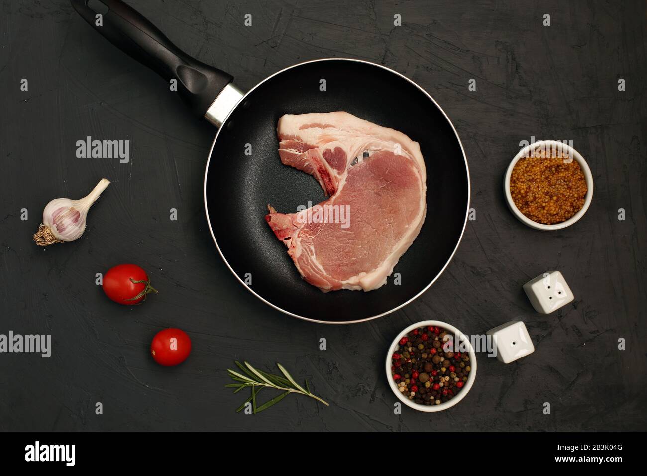 Raw pork loin chops in rustic skillet on black background Stock Photo ...
