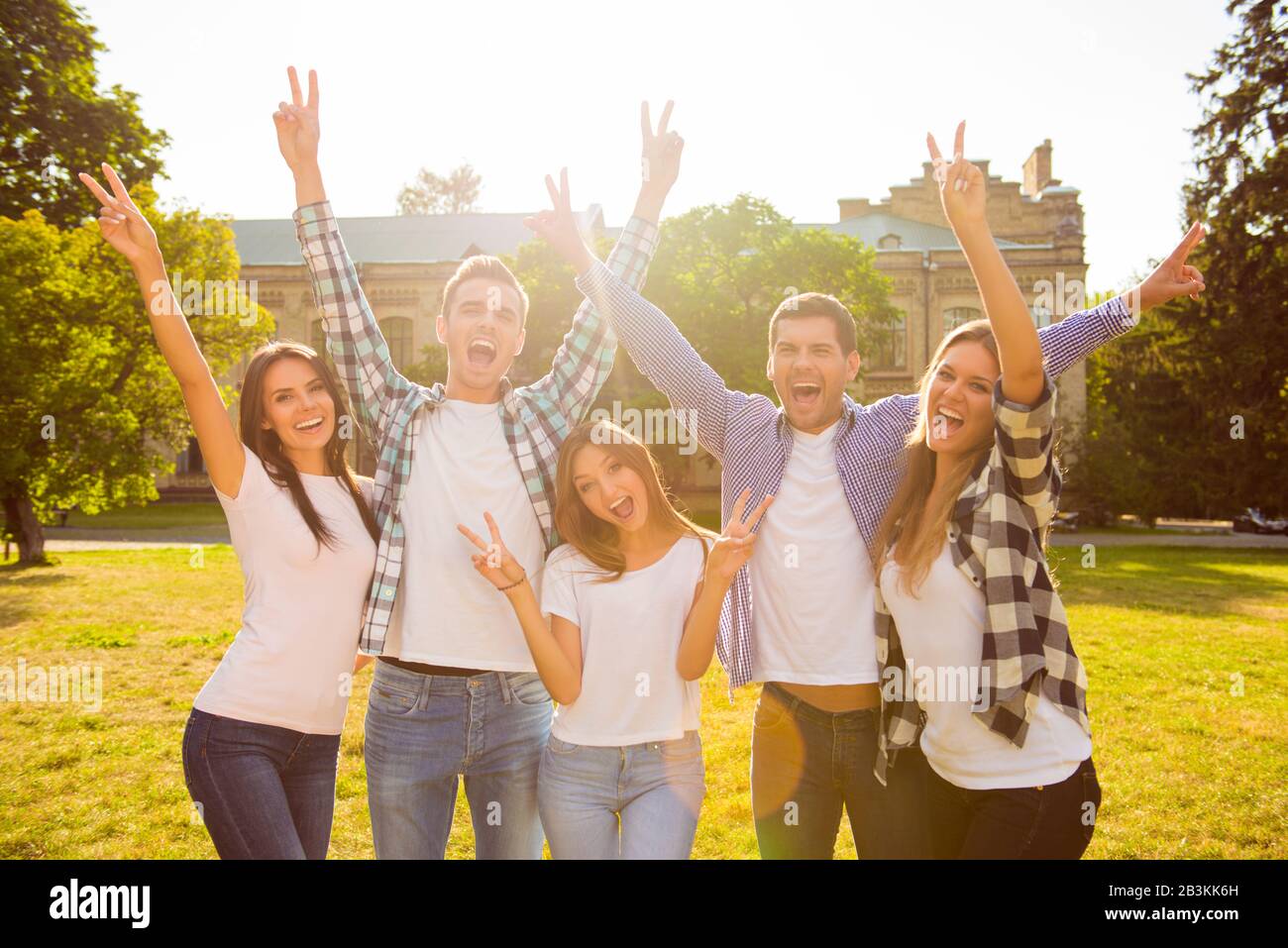 five cheerful best friends having fun and rise hands with gesture v ...
