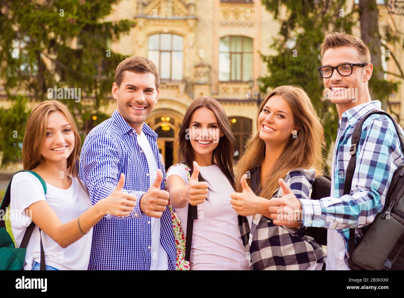 diverse five joyful friends showing thumbs up standing near campus ...
