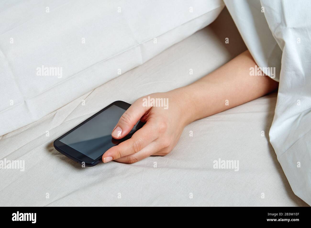 Young woman under duvet with smart phone. Girl sleeping in bed and ...