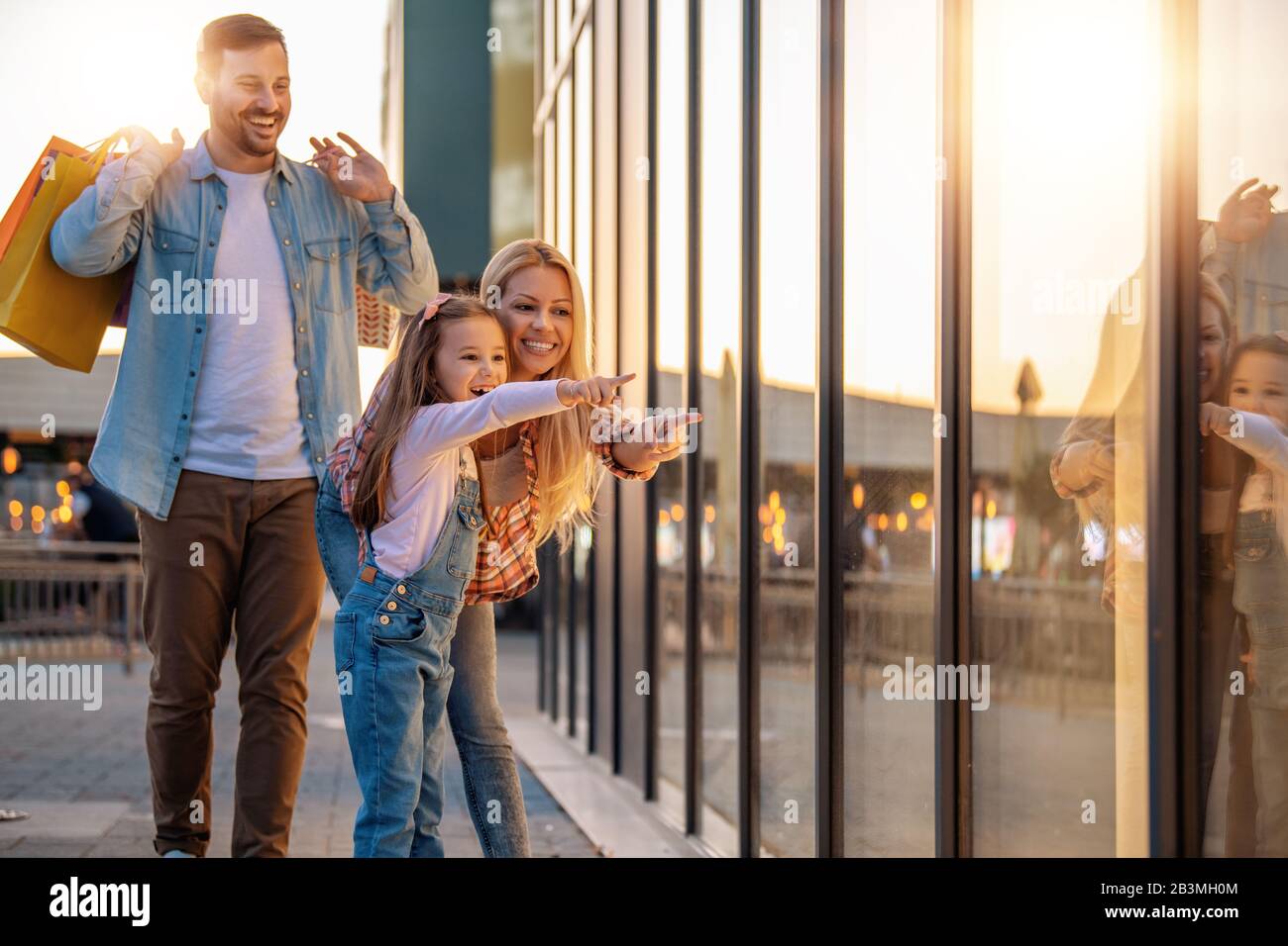 Happy young parents and their daughter are holding shopping bags and ...