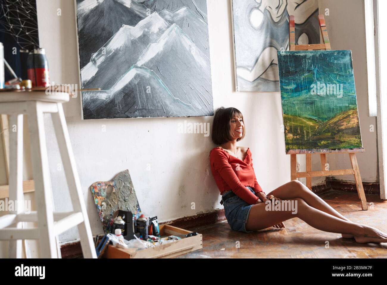 Beautiful happy young woman artist sitting in the art studio, relaxing ...