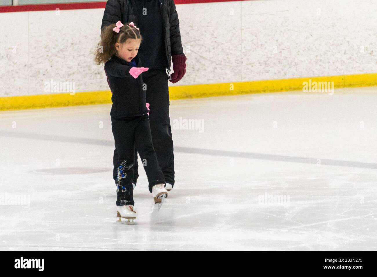 Little girl practicing figure skating moves on the indoor ice rink ...