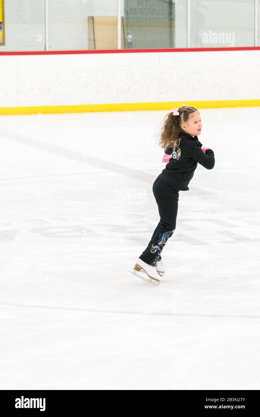 Little girl practicing figure skating moves on the indoor ice rink ...