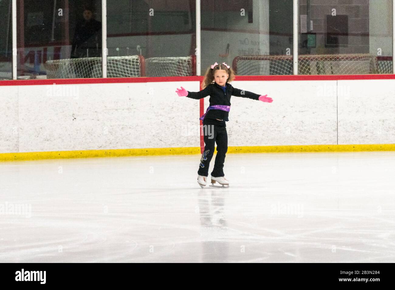 Little girl practicing figure skating moves on the indoor ice rink ...
