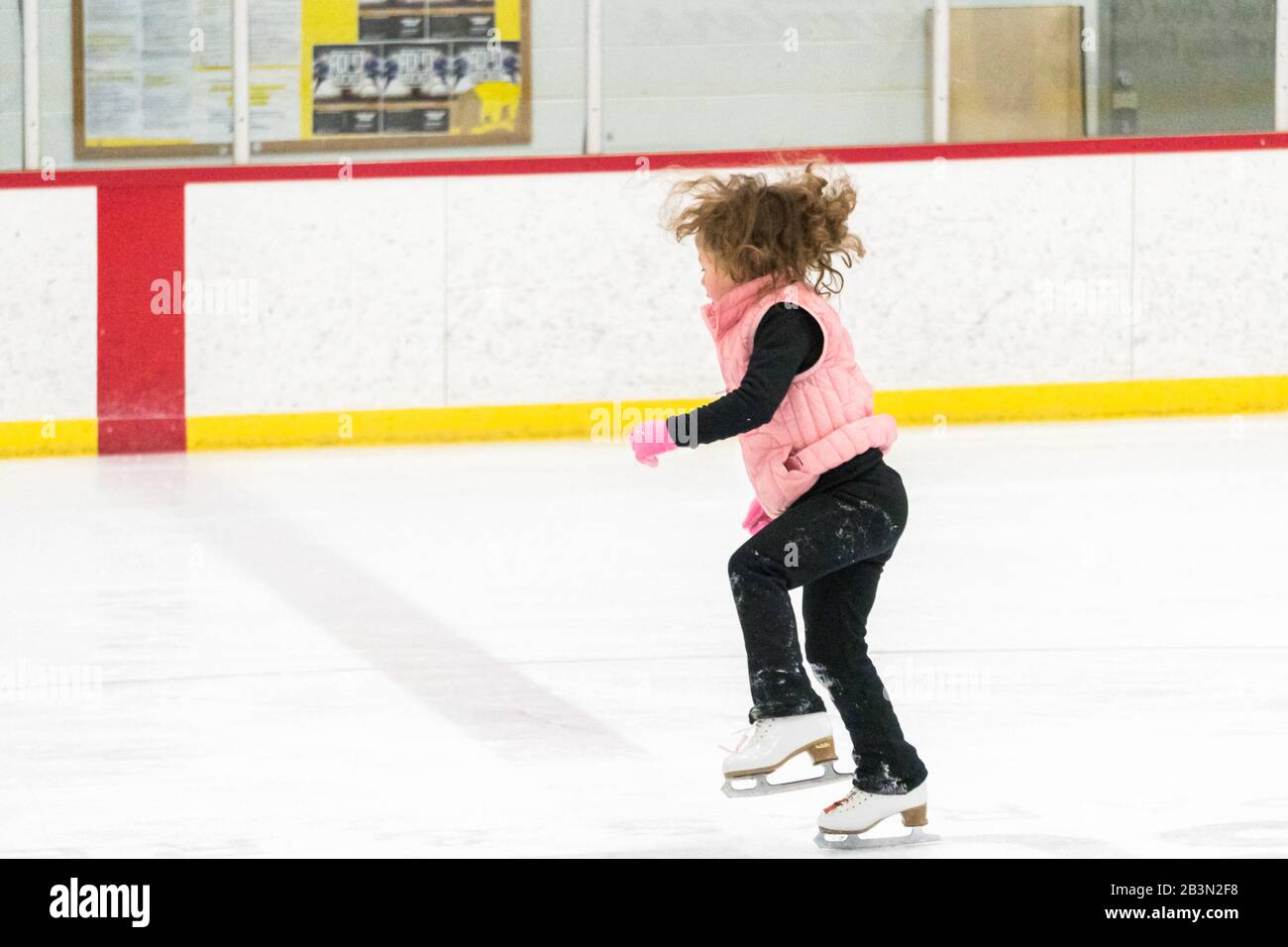 Little girl practicing figure skating moves on the indoor ice rink ...