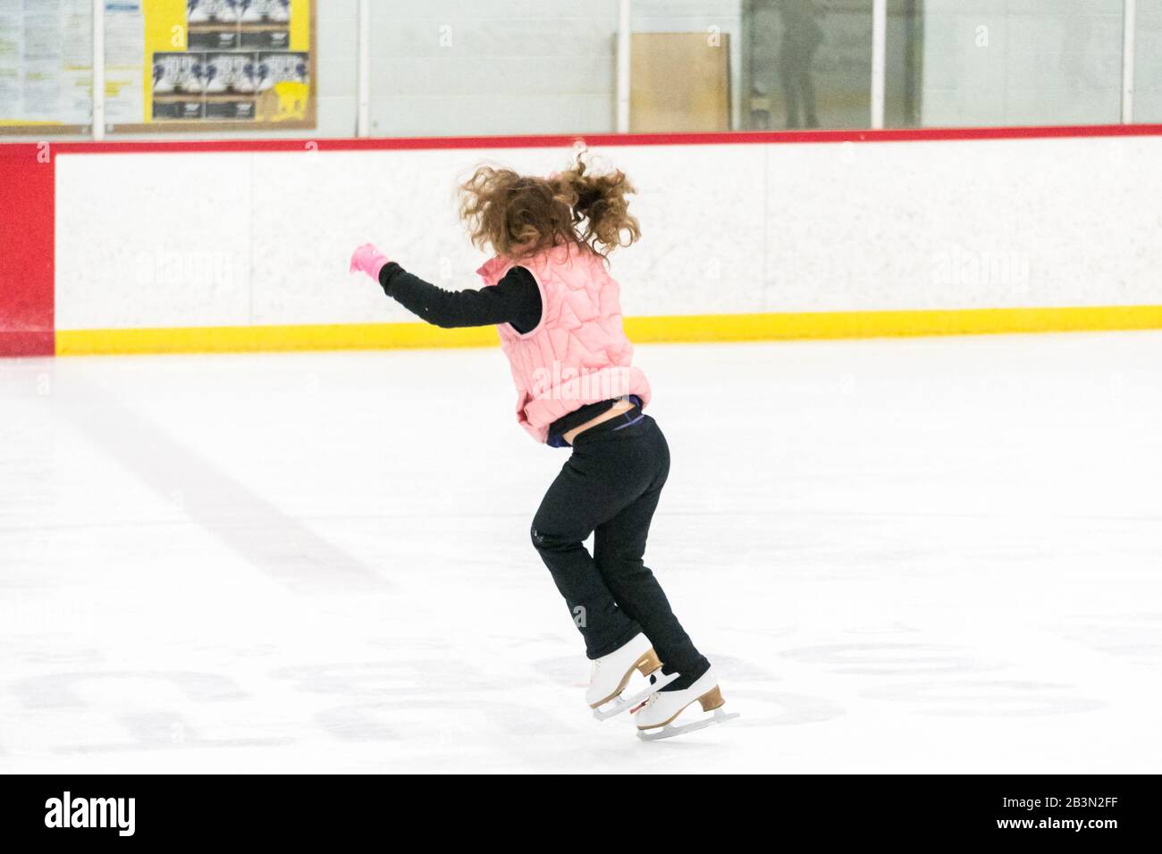 Little girl practicing figure skating moves on the indoor ice rink ...