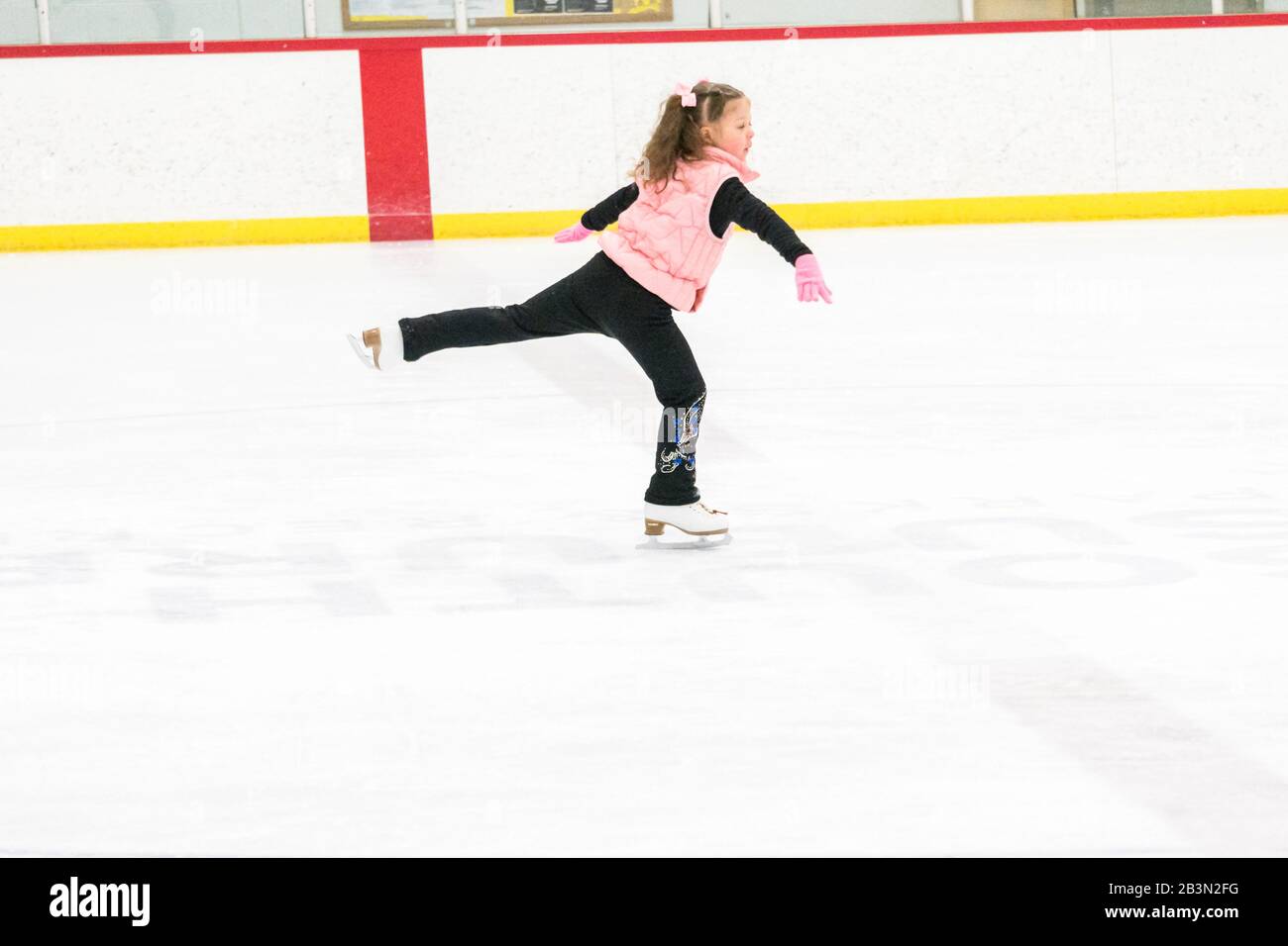 Little girl practicing figure skating moves on the indoor ice rink ...