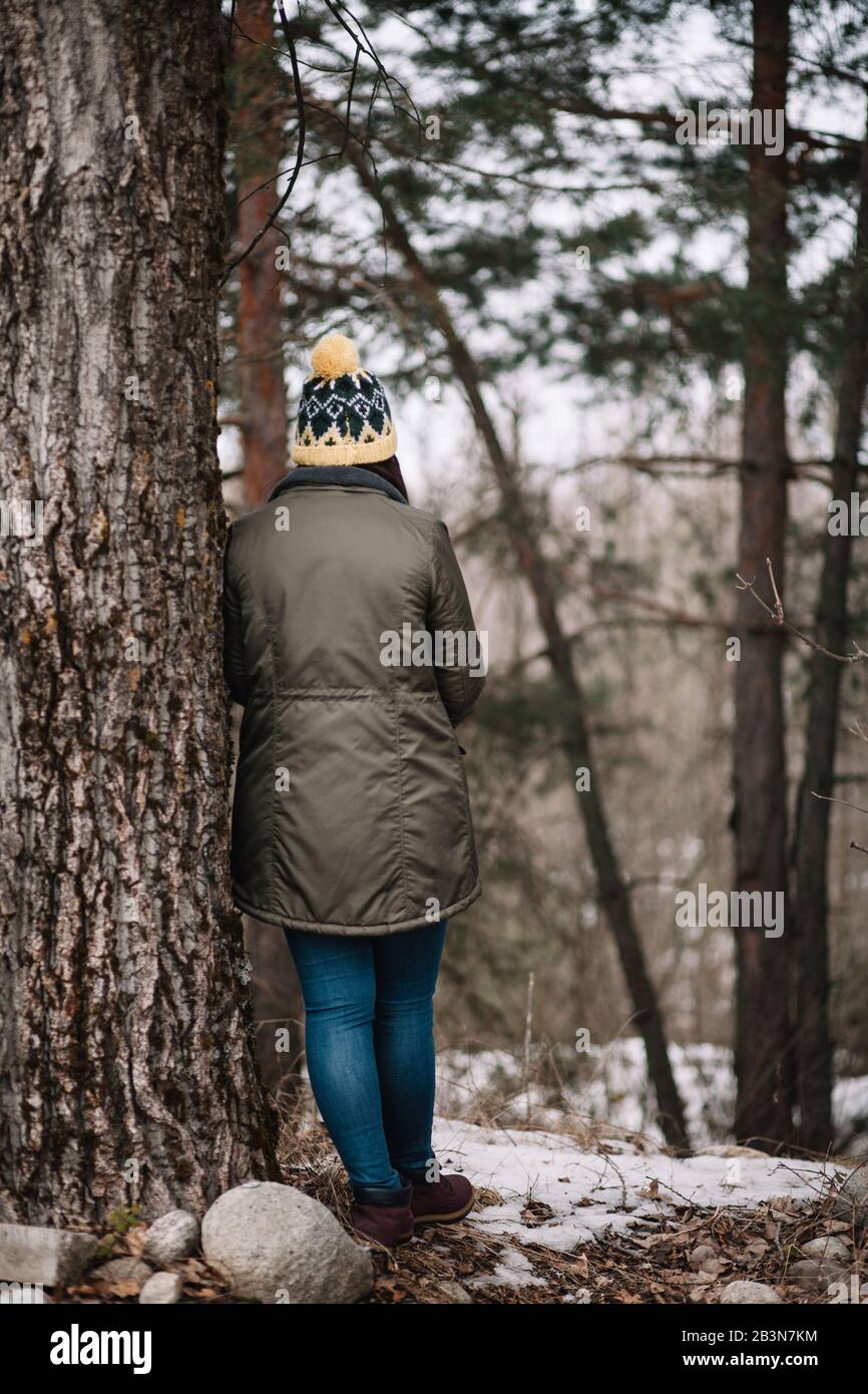 Back of a girl leaning on big tree. Back view of a girl wearing jacket ...