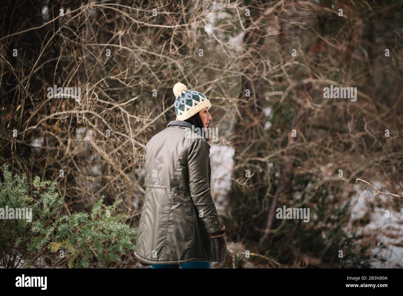 Woman walking in forest in winter clothes. Side view of a woman wearing ...