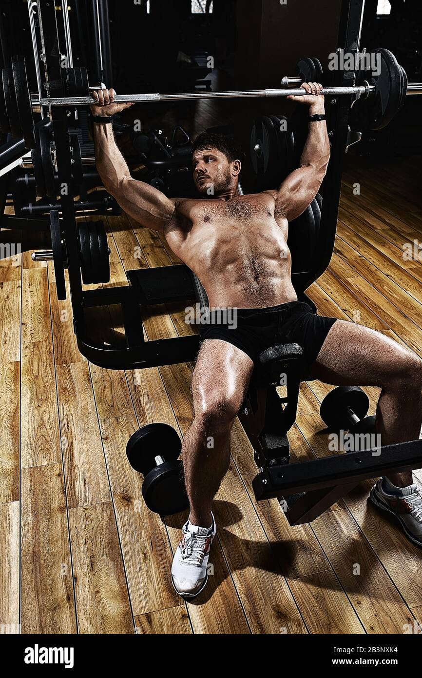 Young muscular man lifting a barbell bench press in the gym. Beautiful ...
