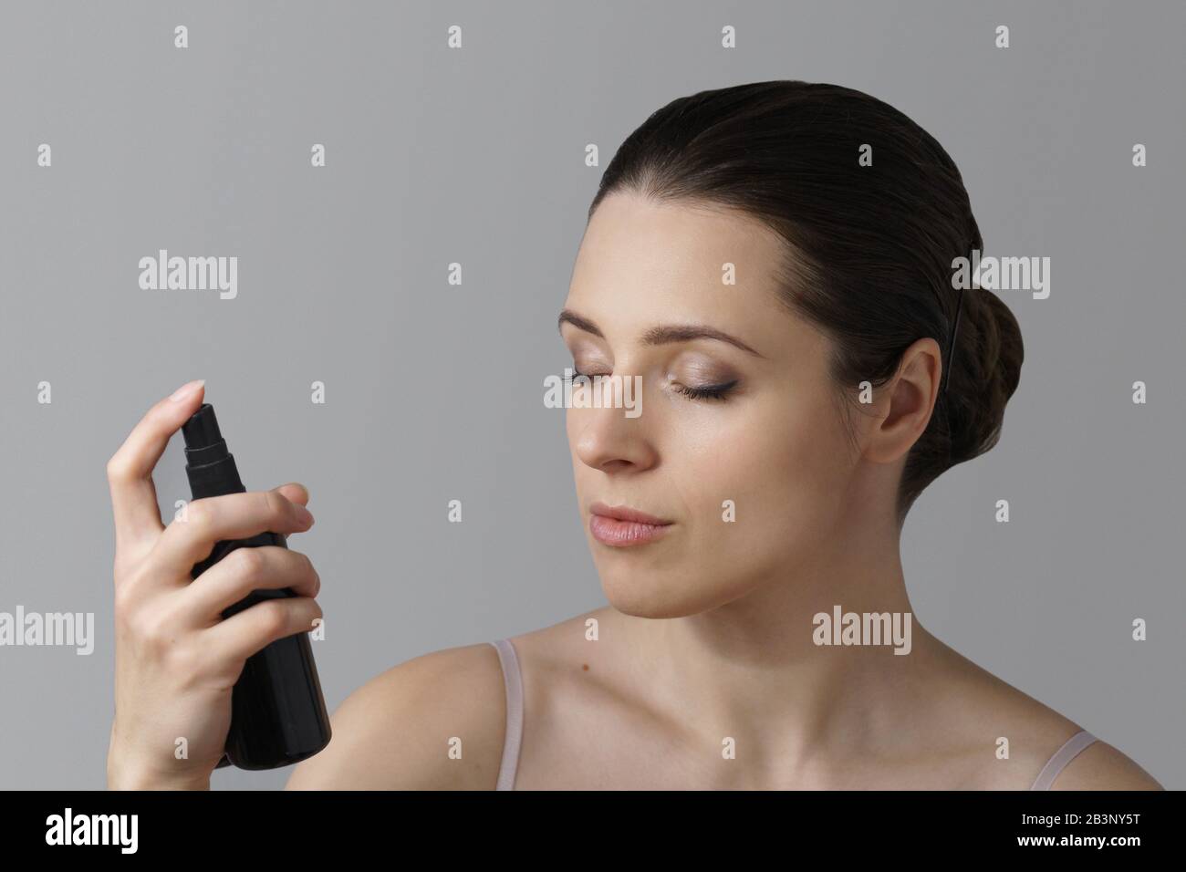 Portrait of brunette woman using spray in black glass bottle over her ...