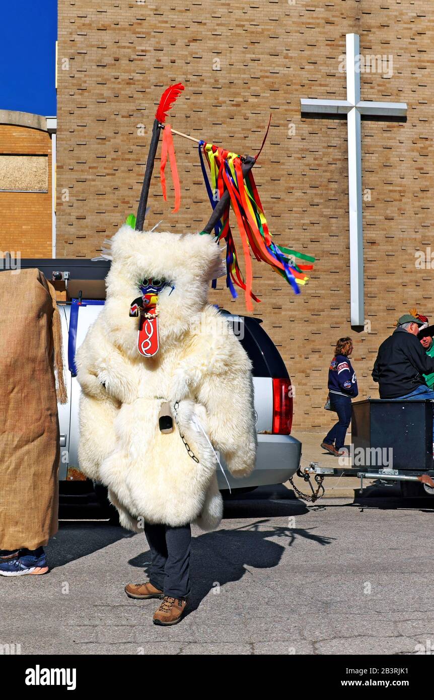 A white Kurent, also known as Kurenti, walks past a church with an ...