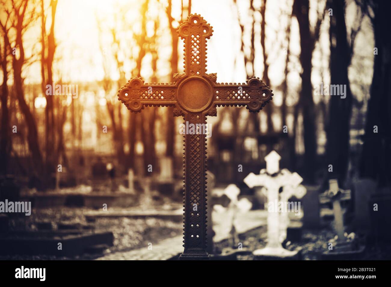 A beautiful old rusty cross stands in a large dark cemetery against a ...