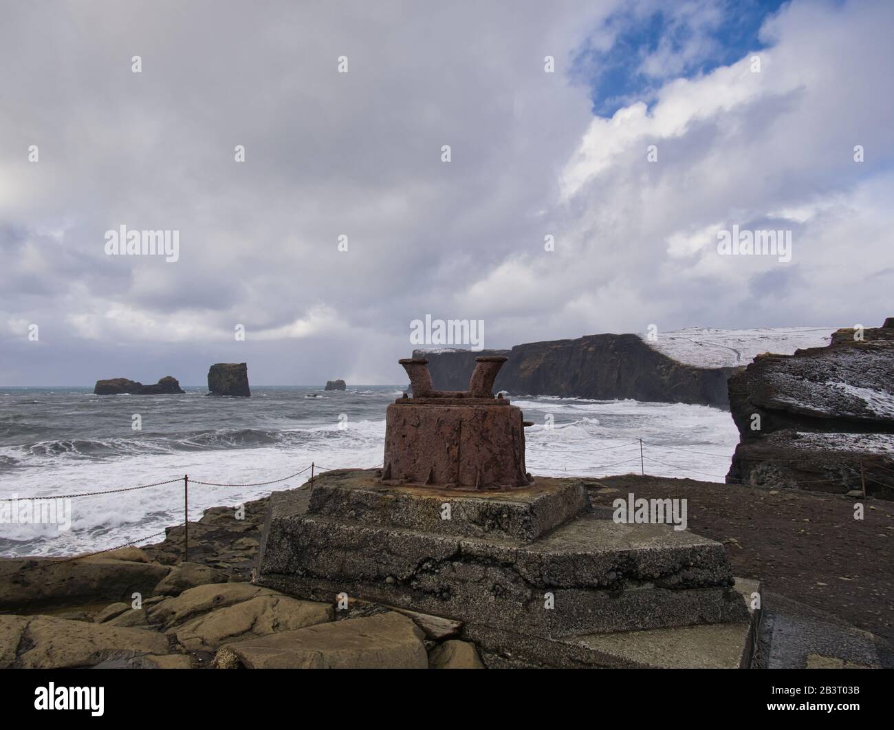 A coastal section in Iceland with a rusty bollard on a concrete base ...