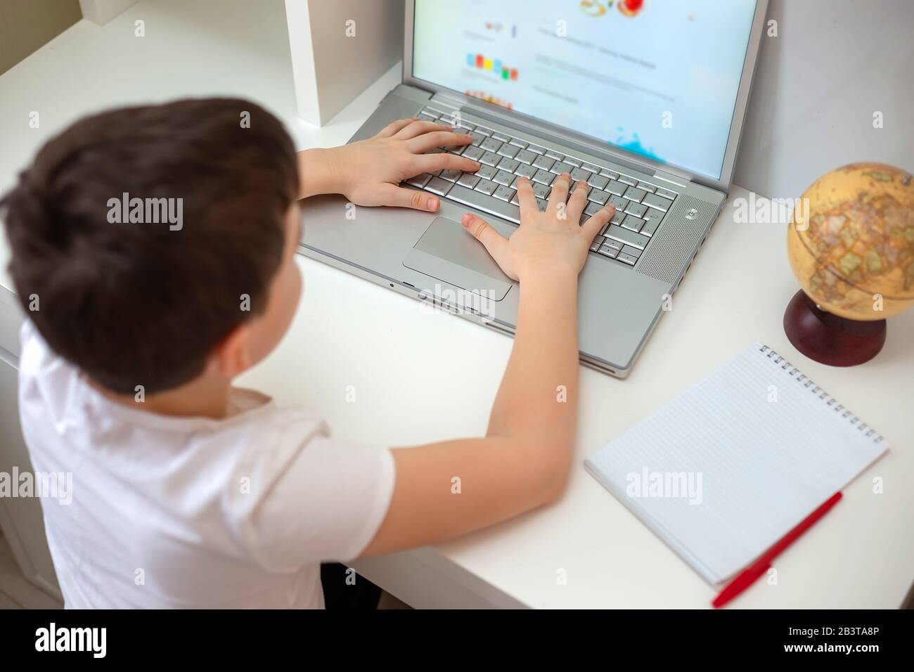 The boy sits with his back behind a laptop, fingers on the keyboard ...
