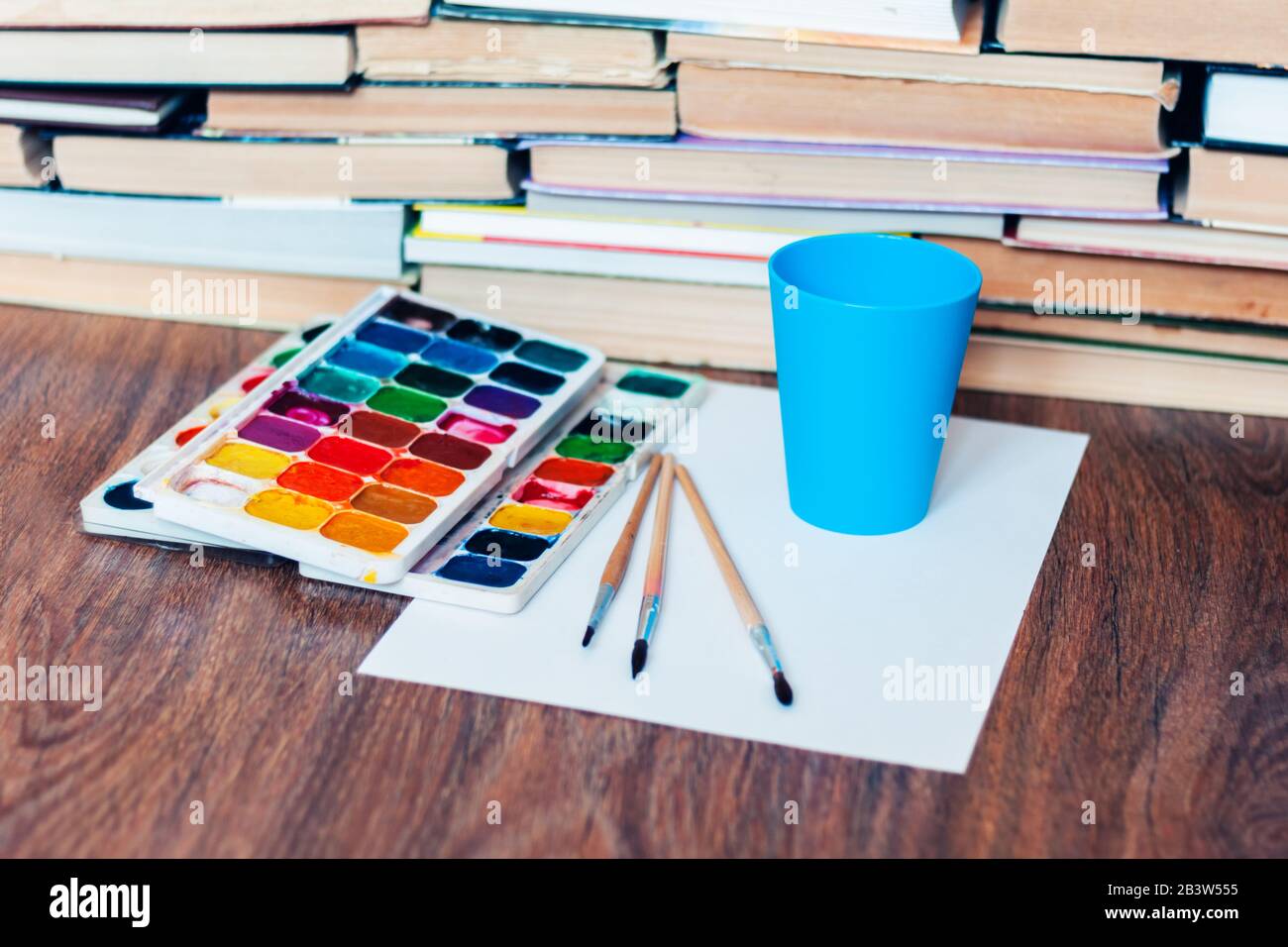 Watercolor paint, brushes well used and sheet of paper on wooden table ...